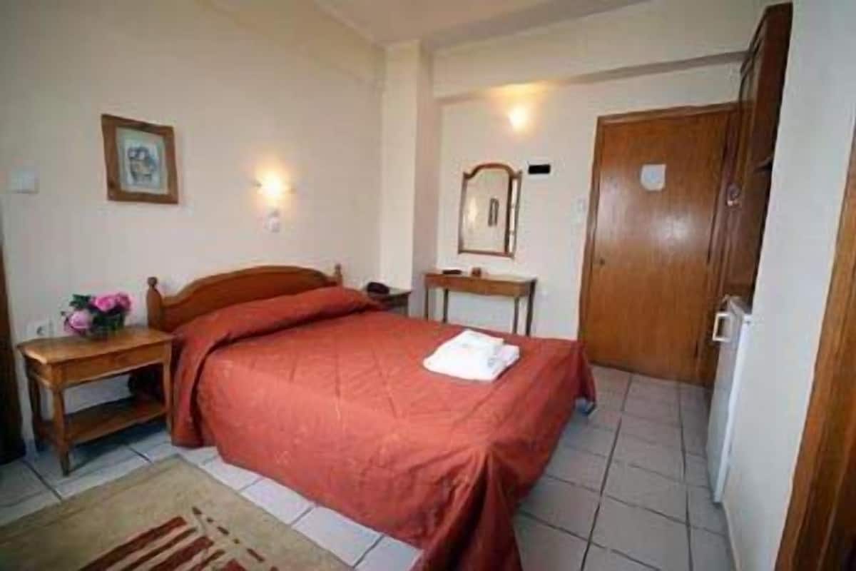 Quarto com cama, escrivaninha de madeira, cadeira, espelho e porta.