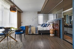 Um quarto moderno com uma cama, uma cadeira azul, uma mesa de vidro e um vaso decorativo.