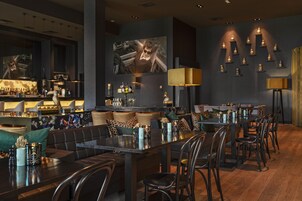 Uma área de bar moderna com um balcão comprido, lugares para sentar e uma grande obra de arte pendurada na parede.
