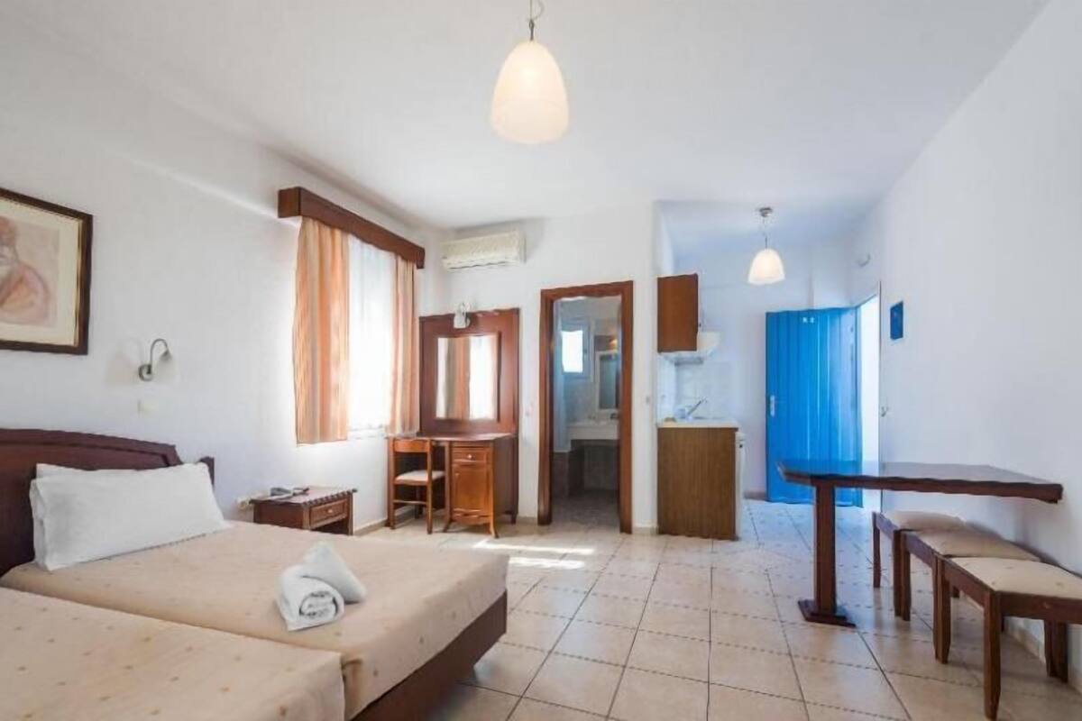 Quarto de hotel com duas camas, uma escrivaninha, uma cadeira, uma mesinha e um banheiro visível por uma porta aberta.