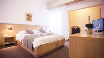 Quarto de hotel com cama, mesa de cabeceira, abajur e televisão.