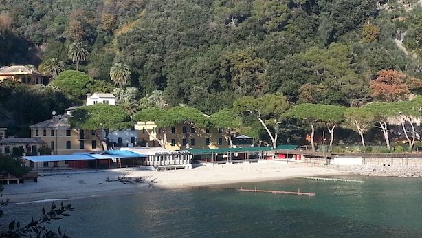 Uma área costeira com edifícios, uma praia e um morro arborizado.