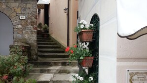 Uma escadaria de pedra estreita leva a um edifício com uma placa que diz “Albergo Hotel Argento”. Há plantas em vasos nos degraus e uma grade de metal no chão.
