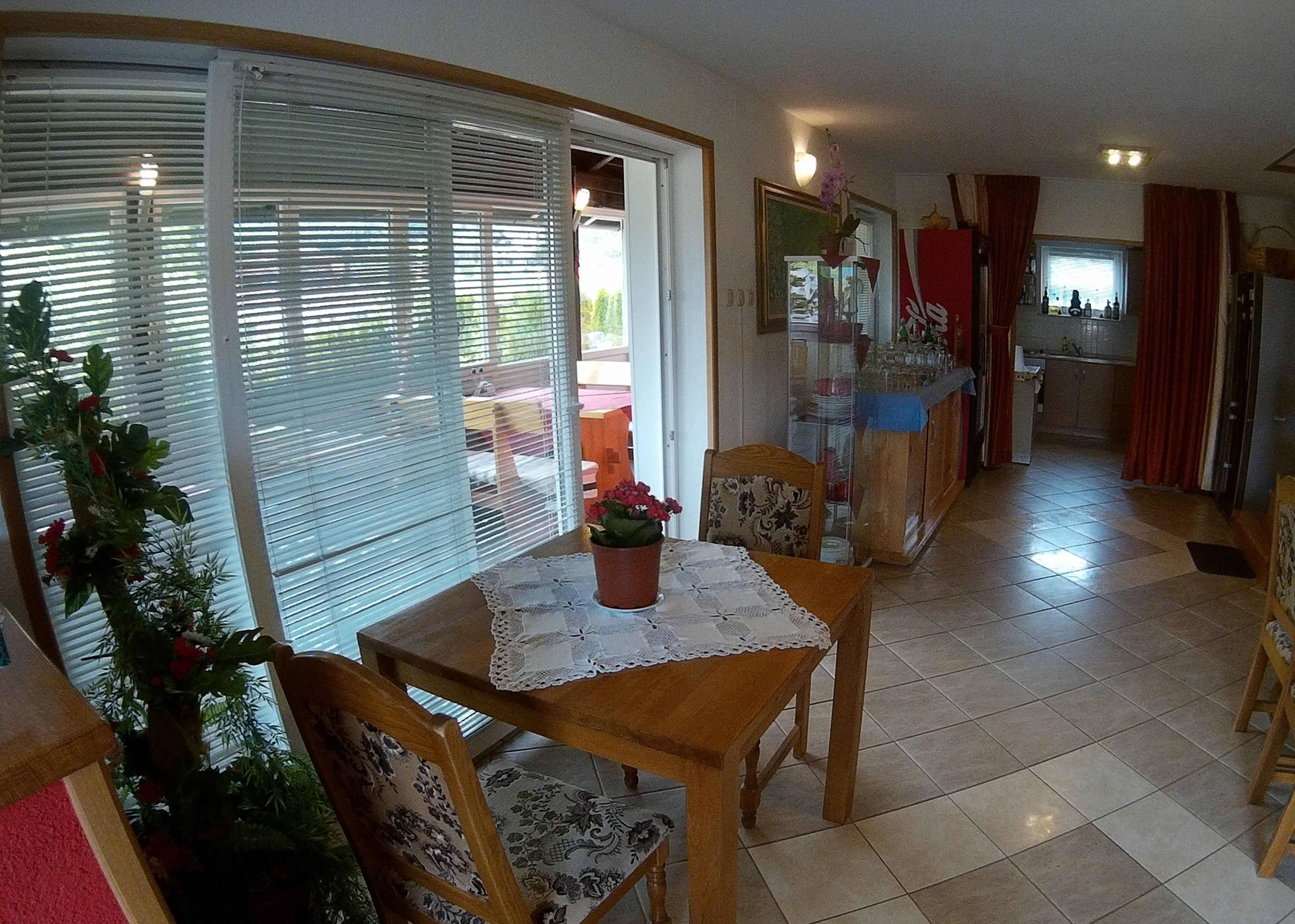 Uma sala de jantar com uma mesa posta para dois, uma planta em vaso e vista para a cozinha.