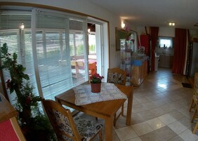 Uma sala de jantar com uma mesa posta para dois, uma planta em vaso e vista para a cozinha.