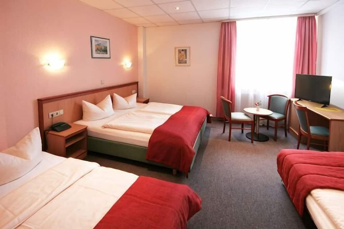 Quarto de hotel com duas camas, uma escrivaninha com cadeira, uma televisão e uma mesinha.