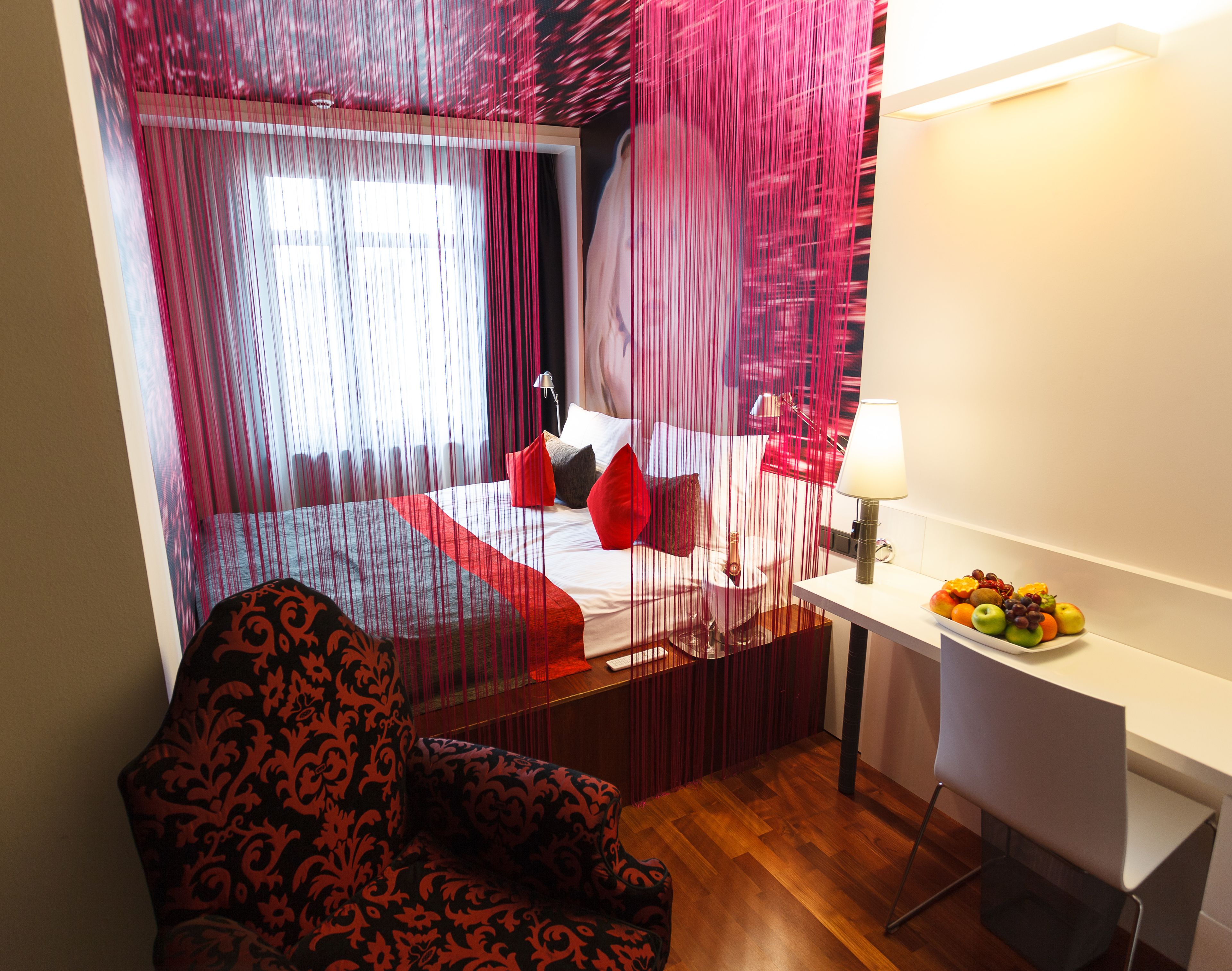 Quarto de hotel com cama, escrivaninha com luminária, cadeira e tigela de frutas.