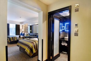 Quarto de hotel com cama, escrivaninha, cadeira e banheiro com espelho e porta-toalhas.
