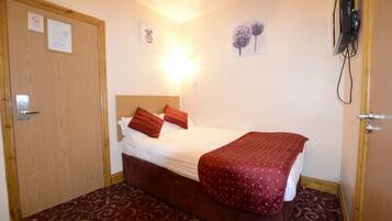 Quarto de hotel com cama, porta de madeira, televisão fixada na parede e carpete estampado.