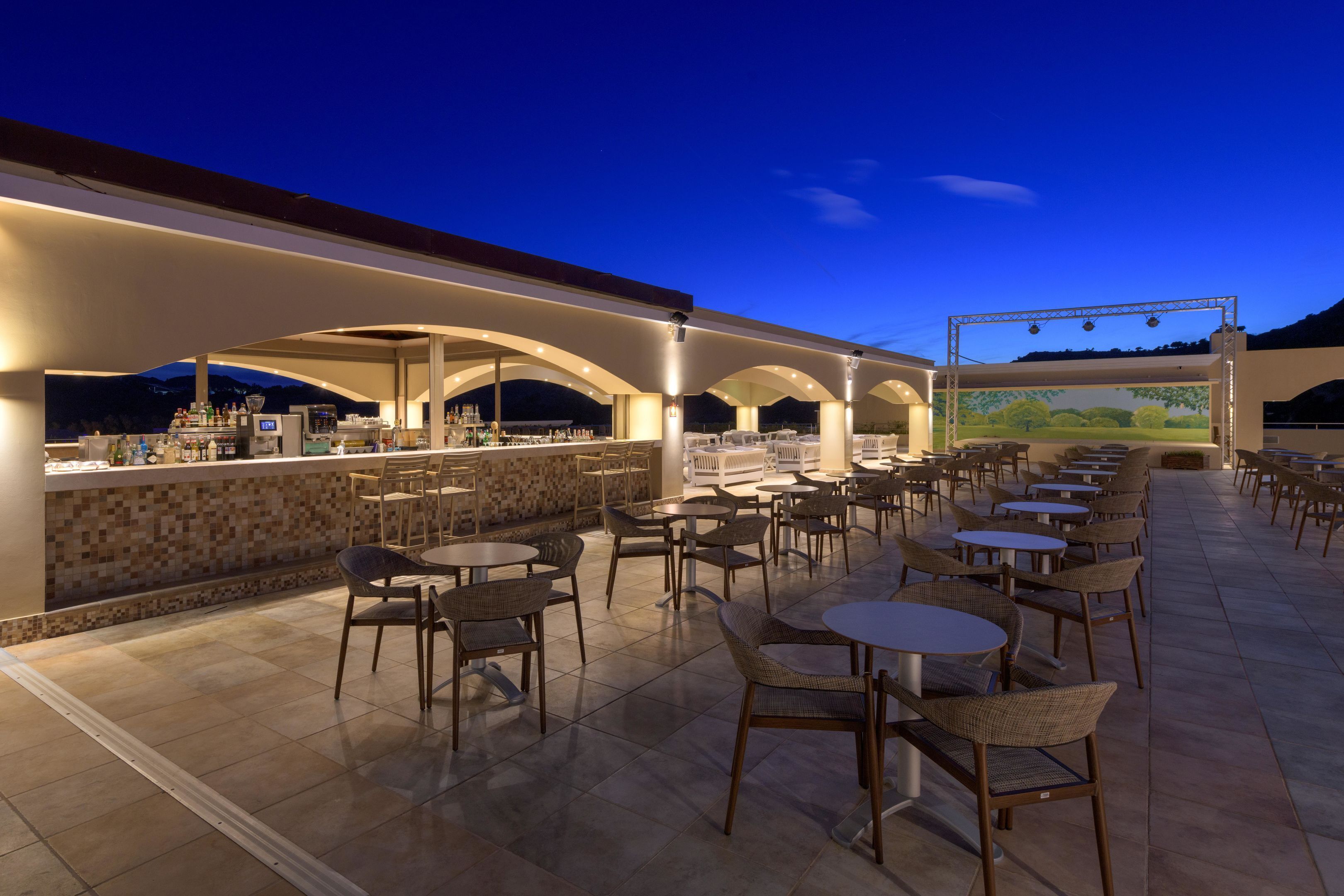 Uma área de refeições ao ar livre com mesas, cadeiras, um bar e vista para as montanhas.