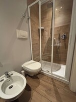 Casa de banho com sanita, bidé e zona de duche com divisória de vidro.