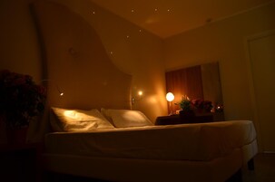 Um quarto com iluminação suave, uma cama, mesa de cabeceira e abajur.