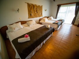 Quarto de hotel com duas camas, uma janela grande e um tapeçaria na parede.