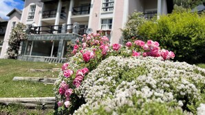 Um edifício de vários andares com varandas, cercado por vegetação exuberante e plantas floridas.