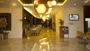 Um saguão de hotel com um balcão de recepção comprido, várias mesas de jantar e luminárias esféricas penduradas.
