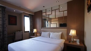 Quarto de hotel com uma cama grande, duas mesas de cabeceira com luminárias, uma escrivaninha e uma cadeira.