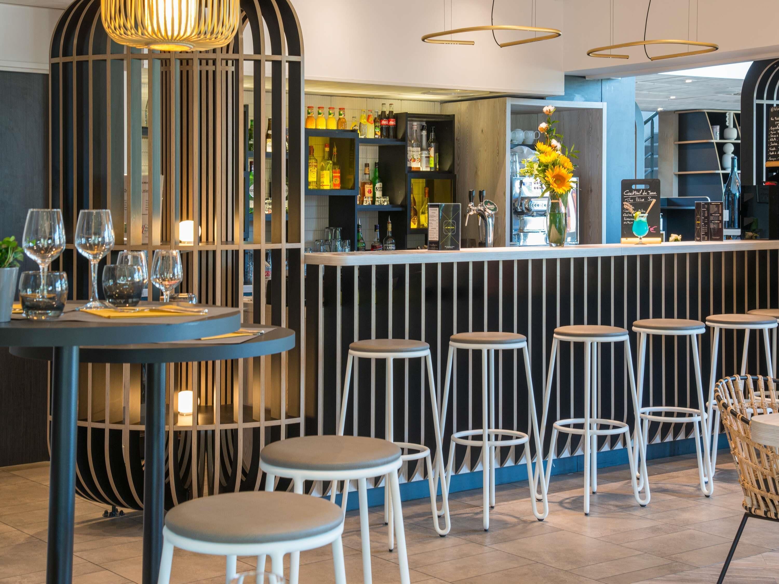 Uma área de bar com banquetas, um balcão com garrafas e uma planta decorativa.