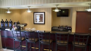 Uma área de bar com balcão, banquetas e uma televisão na parede.