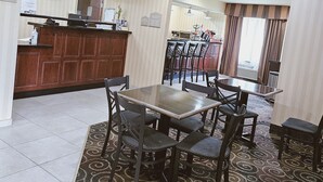 Uma sala de jantar de hotel com uma mesa central e cadeiras, um balcão com espelho e um tapete estampado.