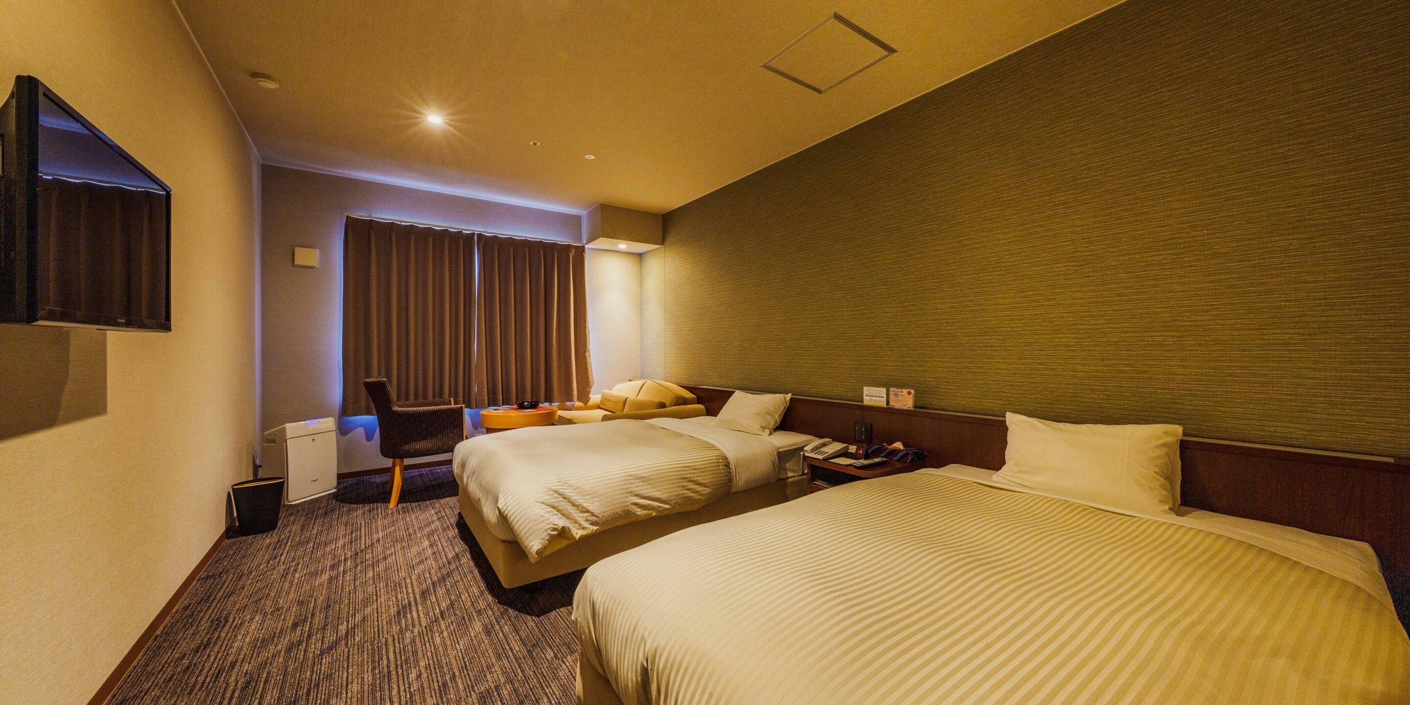 Quarto de hotel com duas camas, uma escrivaninha, uma cadeira e uma televisão.