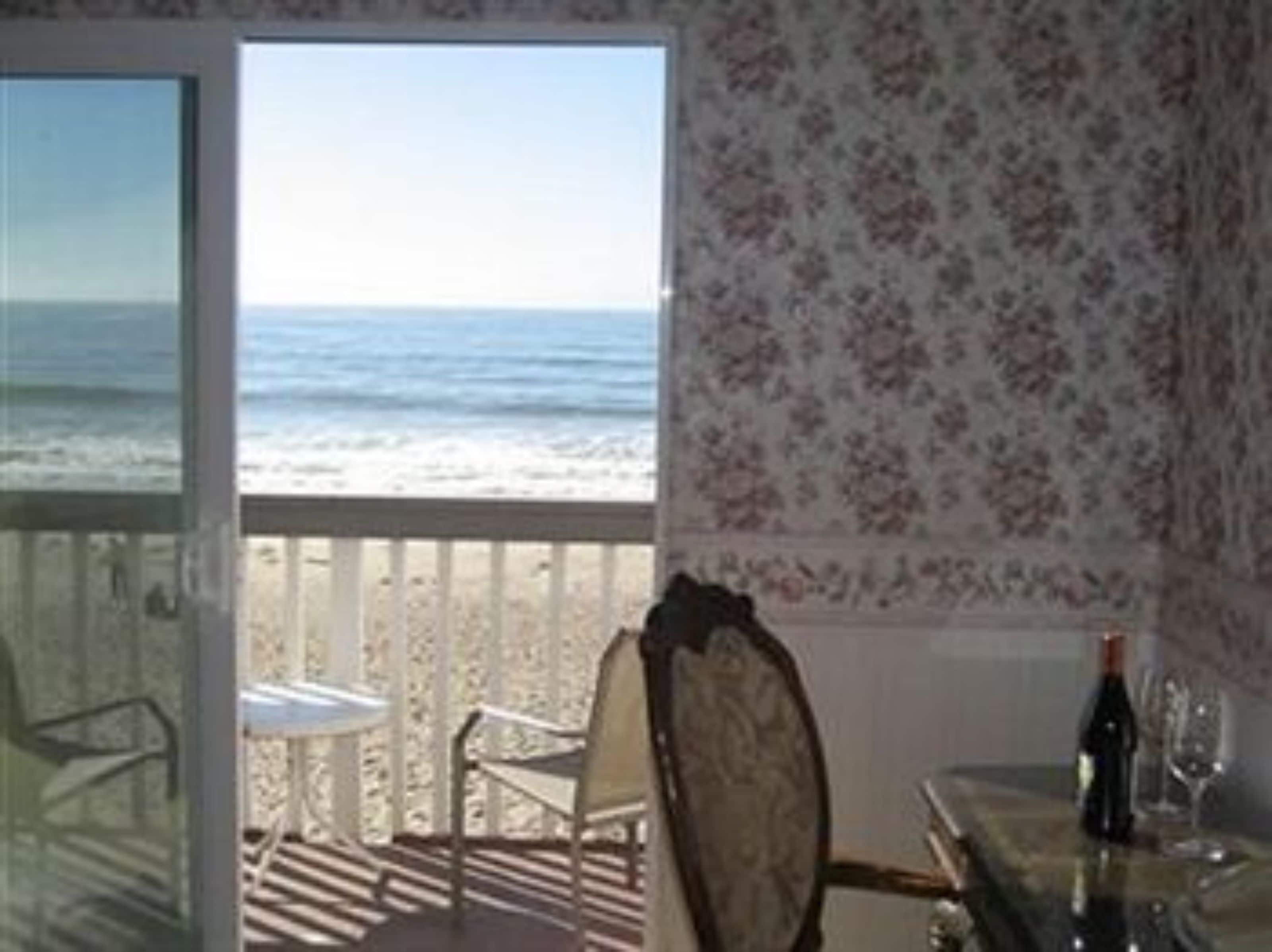 Quarto com vista para o oceano, uma mesa de jantar com cadeiras e uma garrafa de vinho.