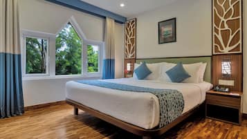 Quarto de hotel com uma cama grande, piso de madeira, janela com cortinas, mesa de cabeceira com telefone e obra de arte pendurada na parede.