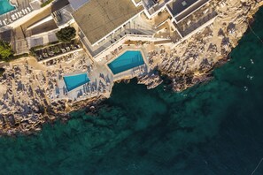 Vista aérea de uma propriedade costeira com várias piscinas, um trecho de costa rochosa e um caminho pavimentado.