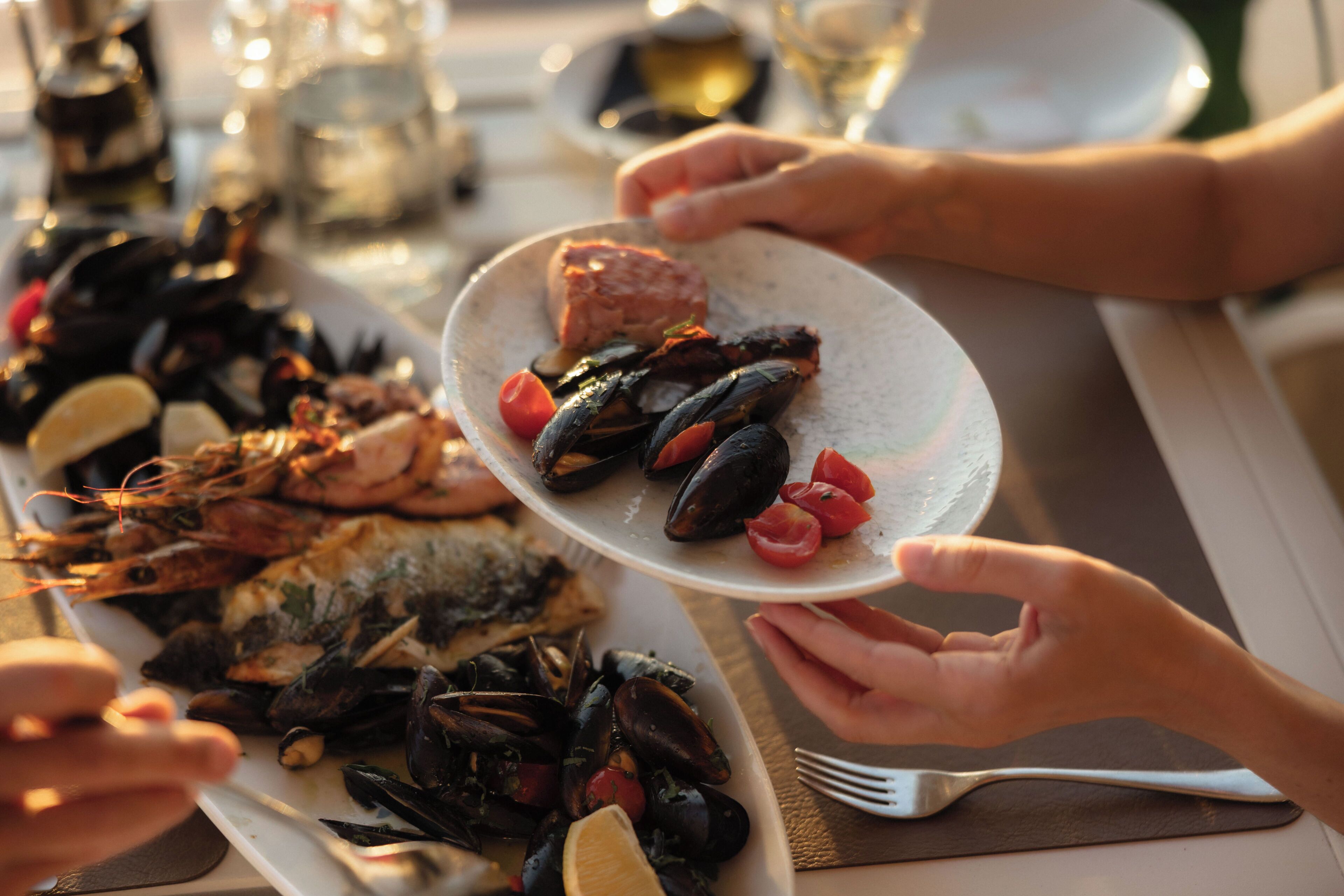 Uma mesa de jantar com pratos de frutos do mar, incluindo mexilhões e camarões, e uma taça de vinho.
