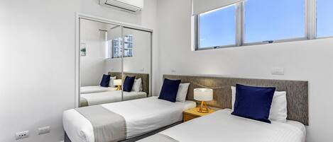 Quarto de hotel com duas camas, um espelho grande, uma janela e um aparelho de ar condicionado.
