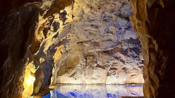 Visão do interior de uma caverna com uma piscina refletora no fundo.