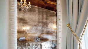 Quarto rústico com teto de madeira, cama com colchão texturizado e um lustre.