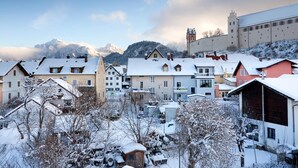 Uma vila coberta de neve com edifícios tradicionais e um castelo ao fundo.