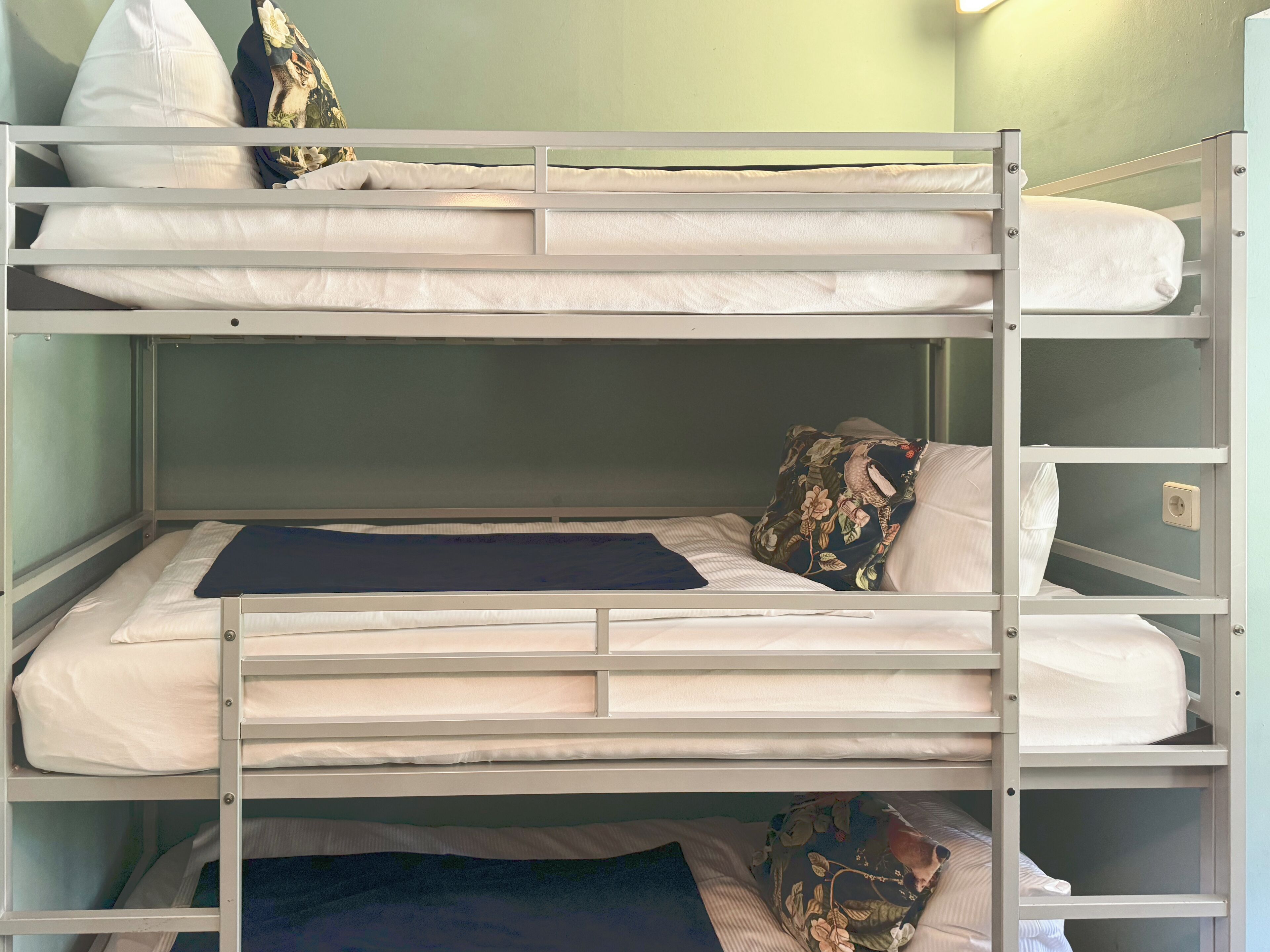 Uma cama beliche com três andares, cada um com roupa de cama branca e um travesseiro.