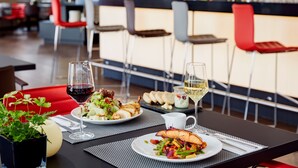 Uma mesa de jantar com pratos de comida, copos de vinho e um bar ao fundo.