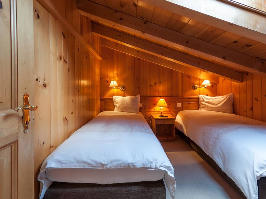 Quarto de cabana de madeira com duas camas, paredes de madeira e duas luminárias fixadas na parede.