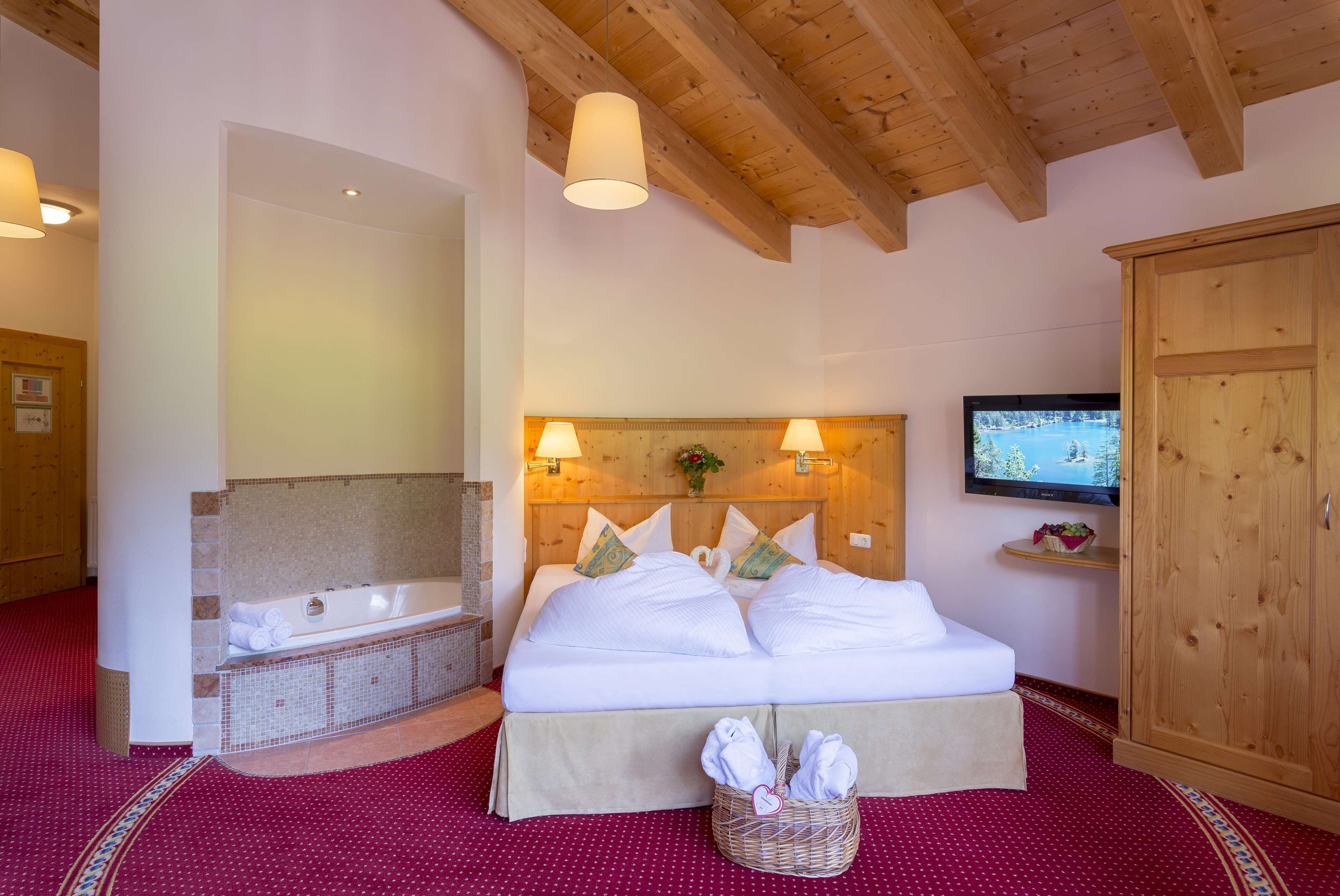 Quarto de hotel com uma cama grande, teto de madeira, televisão na parede e tapete vermelho.