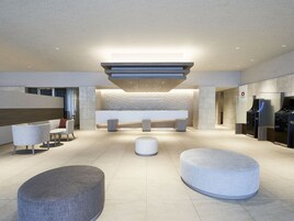 Um lobby de hotel moderno com balcão de atendimento, área de estar e totens de autoatendimento.