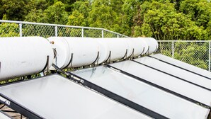 Terraço com painéis solares e grandes tanques cilíndricos, cercado por uma grade de metal e vegetação exuberante.