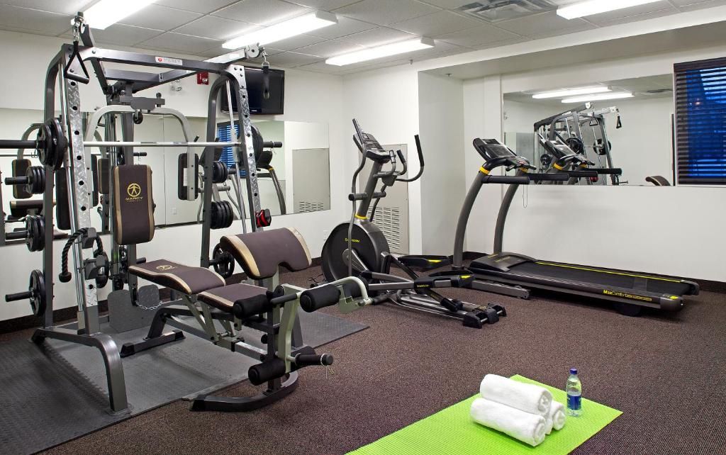 Uma academia com equipamentos de musculação, esteiras e colchonetes.