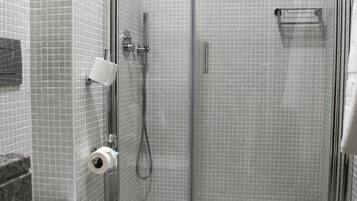 Um banheiro moderno com chuveiro em box de vidro, vaso sanitário branco e piso ladrilhado.