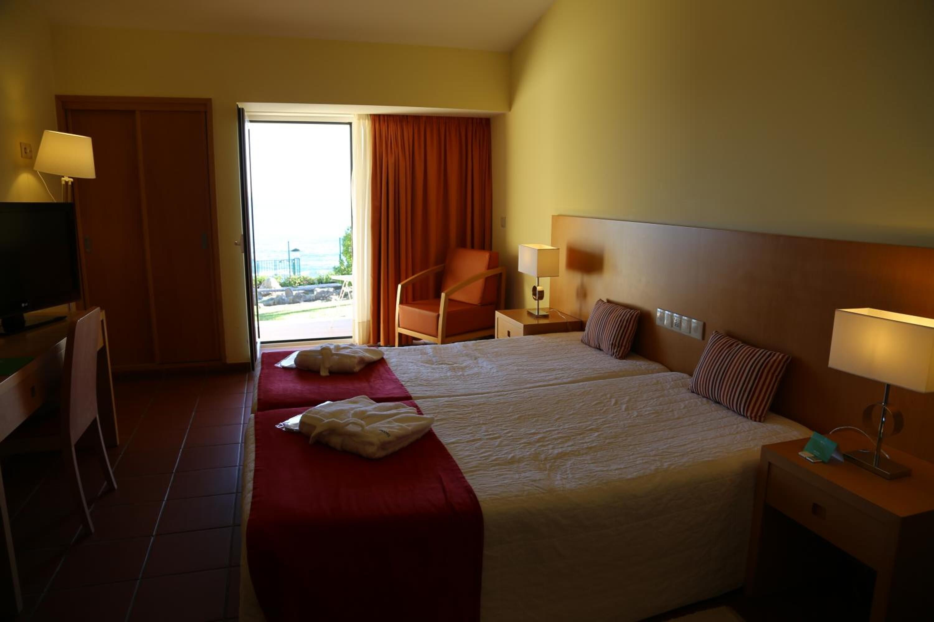 Quarto de hotel com duas camas, uma televisão, uma escrivaninha e uma cadeira.