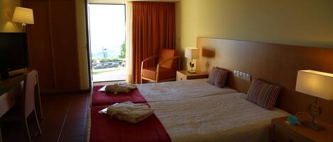 Quarto de hotel com duas camas, uma televisão, uma escrivaninha e uma cadeira.