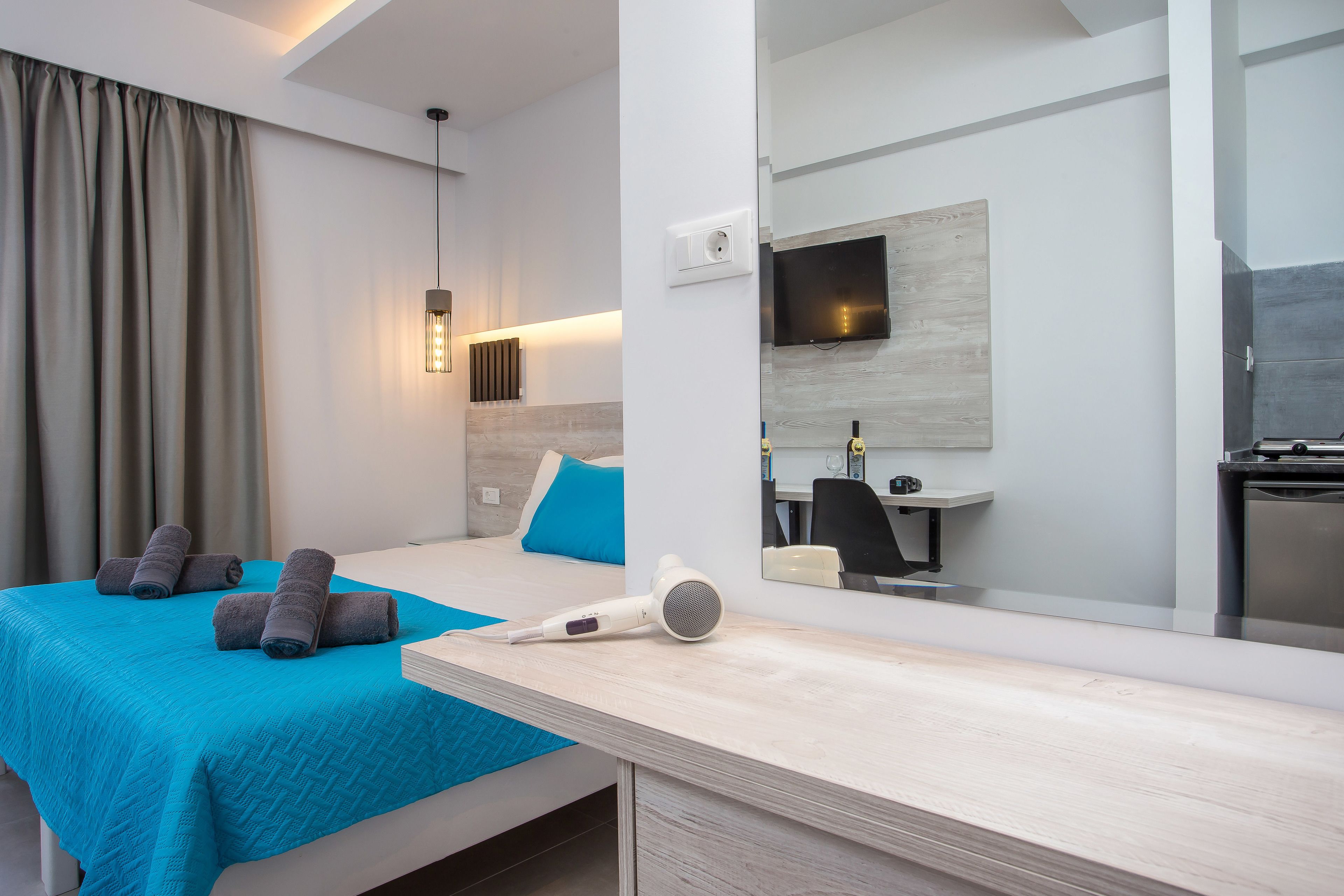Quarto de hotel moderno com uma cama, uma escrivaninha, um espelho e um secador de cabelo na mesa de cabeceira.