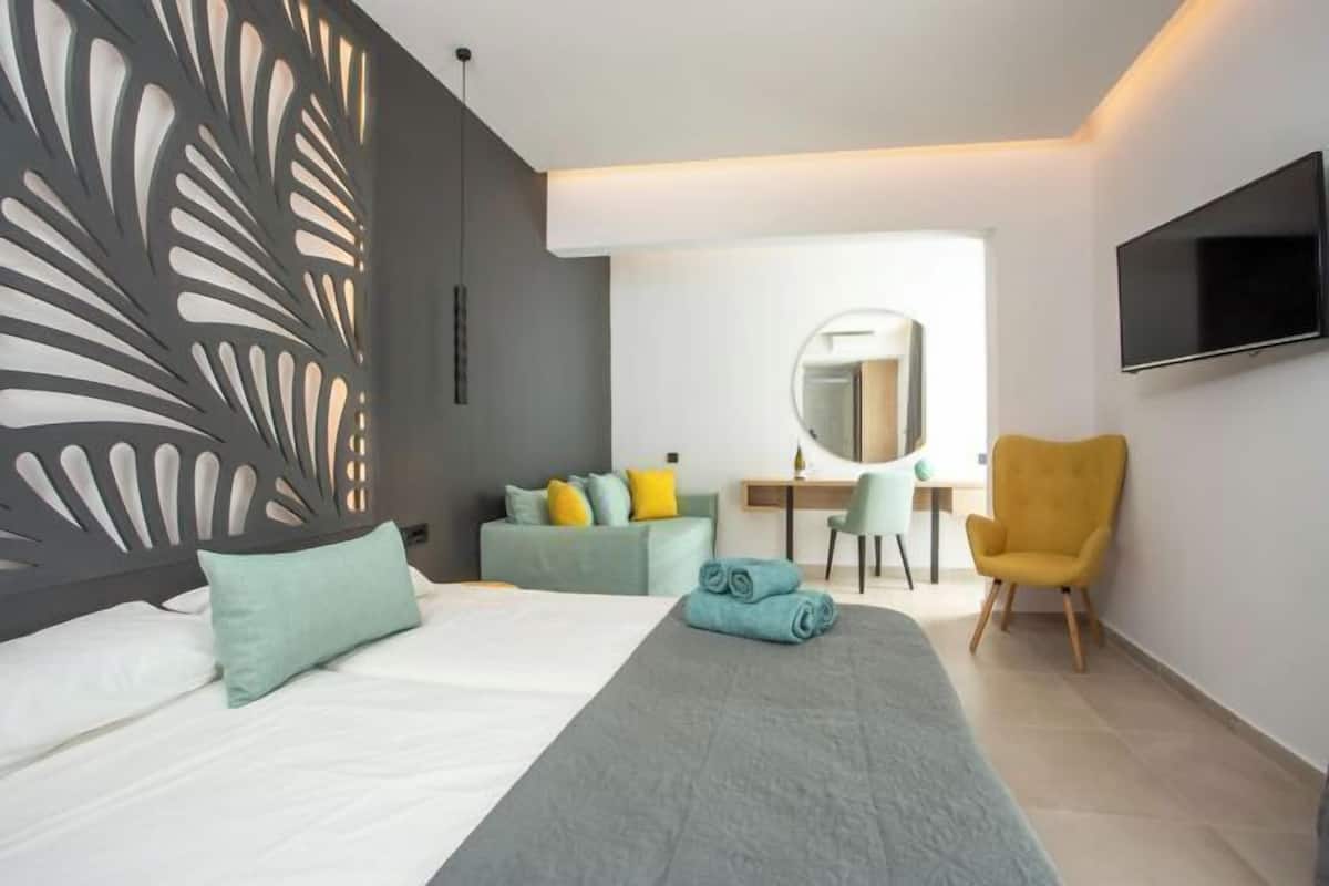 Quarto de hotel moderno com uma cama, uma escrivaninha, uma cadeira, uma televisão e um painel decorativo na parede.