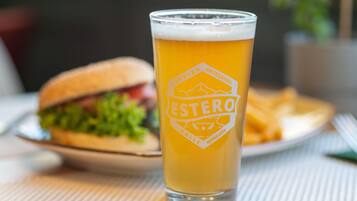 Um copo de cerveja com etiqueta, um hambúrguer e batatas fritas em cima de uma mesa.