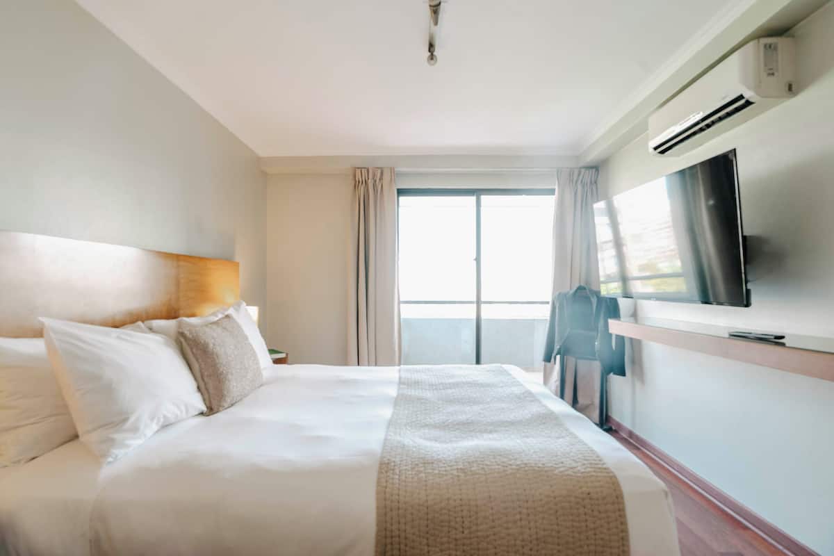 Quarto de hotel com cama, televisão, ar condicionado e janela com cortinas.