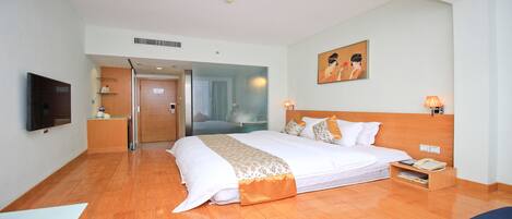 Quarto de hotel com uma cama grande, televisão, mesa de cabeceira de madeira e um quadro na parede.