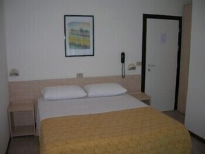 Quarto de hotel com cama, mesa de cabeceira, quadro na parede, telefone e porta.