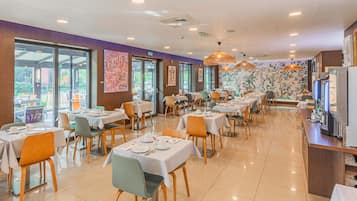 Um restaurante com várias mesas e cadeiras, grandes janelas e chão de azulejos.