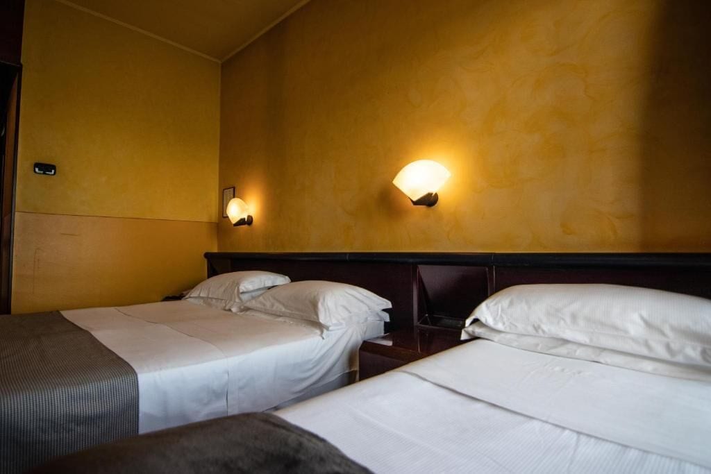 Quarto de hotel com duas camas, um painel de cabeceira de madeira e luminárias fixadas na parede.